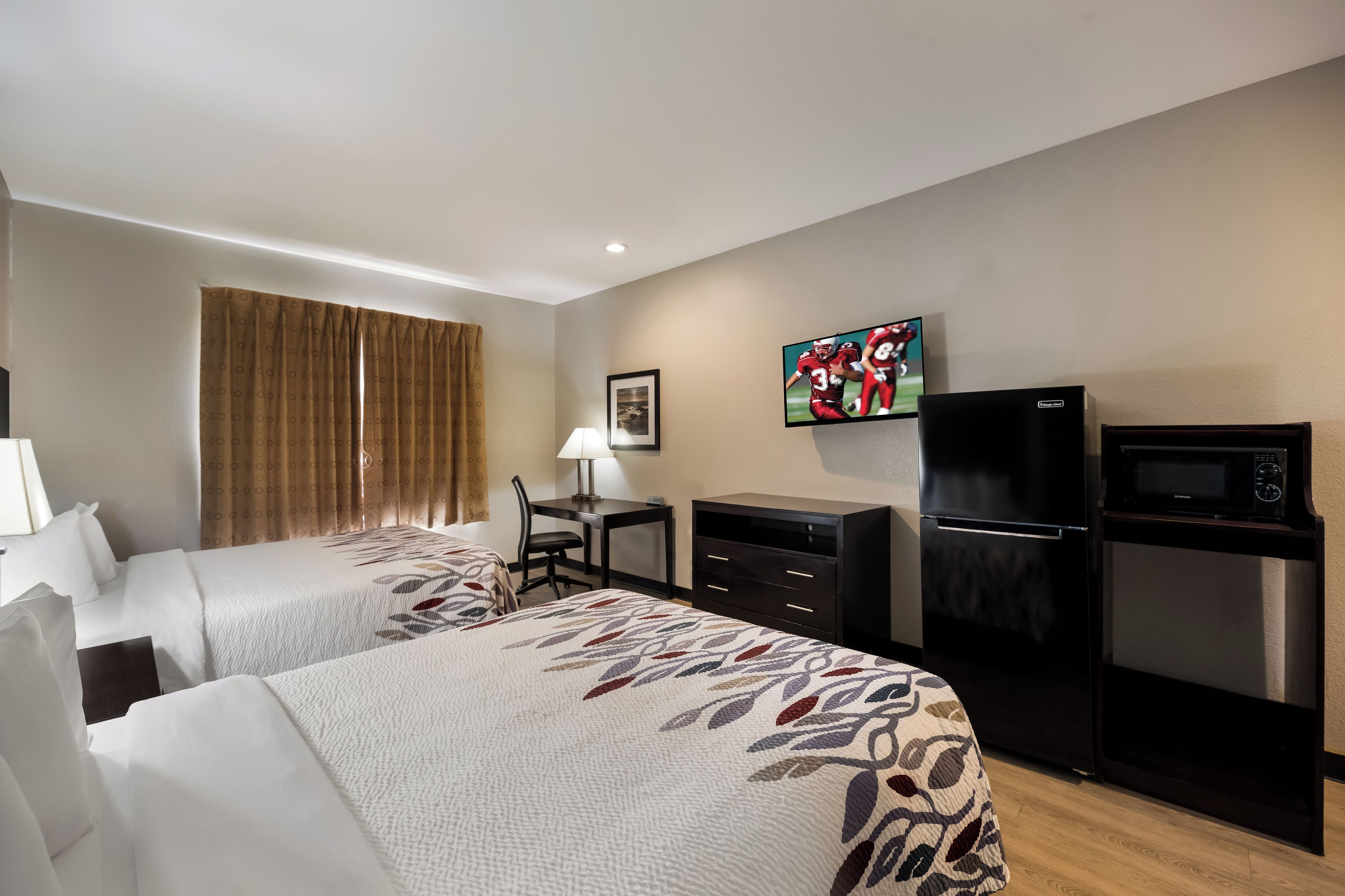 Quarto de hotel com duas camas, uma escrivaninha, frigorífico e televisão.