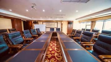 Sala de conferência com uma mesa comprida e várias cadeiras, um quadro branco e um tapete decorativo.