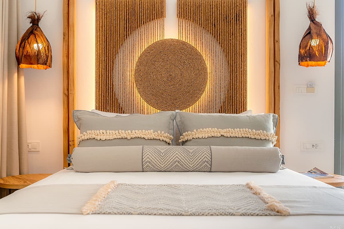 Quarto bem arrumado com uma cama grande, duas luminárias na parede e um painel decorativo tecido.
