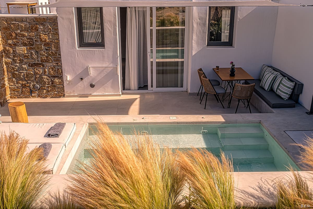 Uma área moderna com piscina ao ar livre, parede de pedra, espaço de estar com mesa e cadeiras, e porta de correr de vidro.
