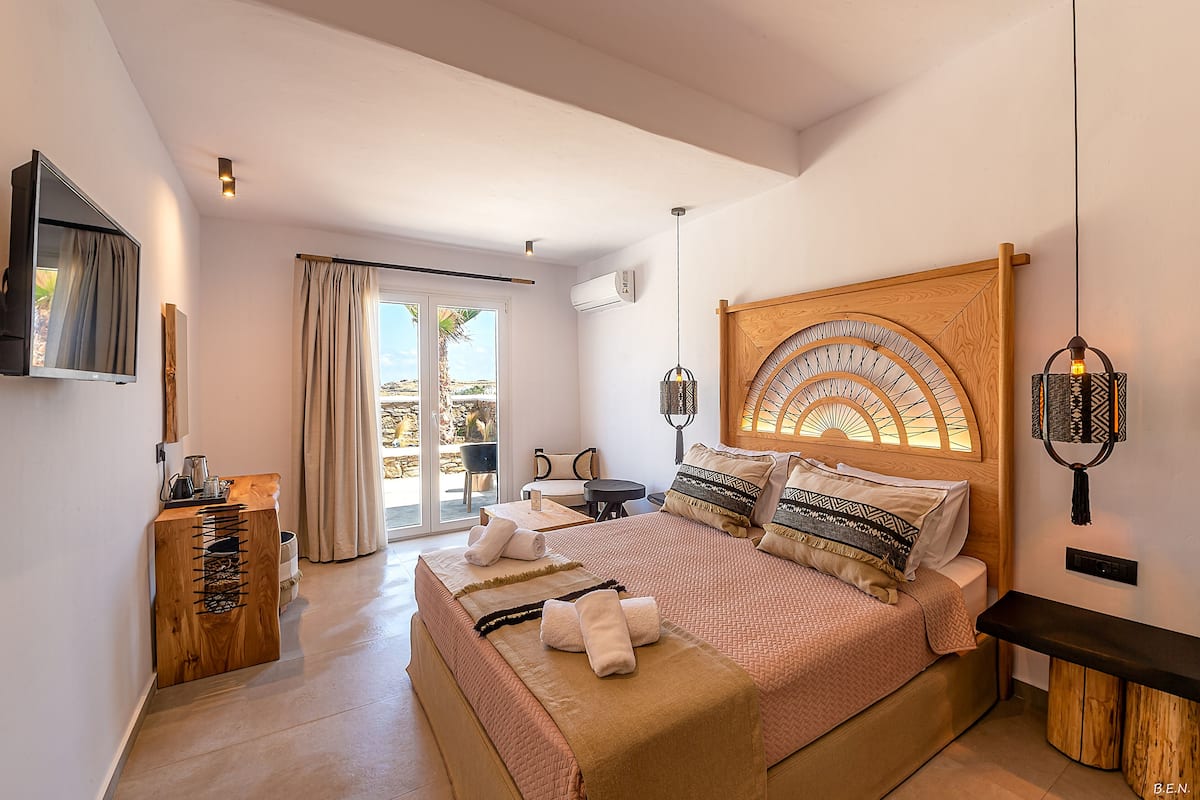 Quarto moderno com cama grande, cabeceira de madeira, televisão e varanda com vista.