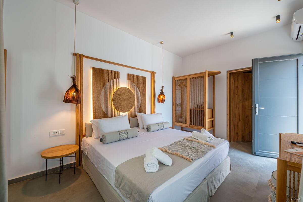 Quarto de hotel moderno com uma cama grande, uma mesinha e um guarda-roupa.