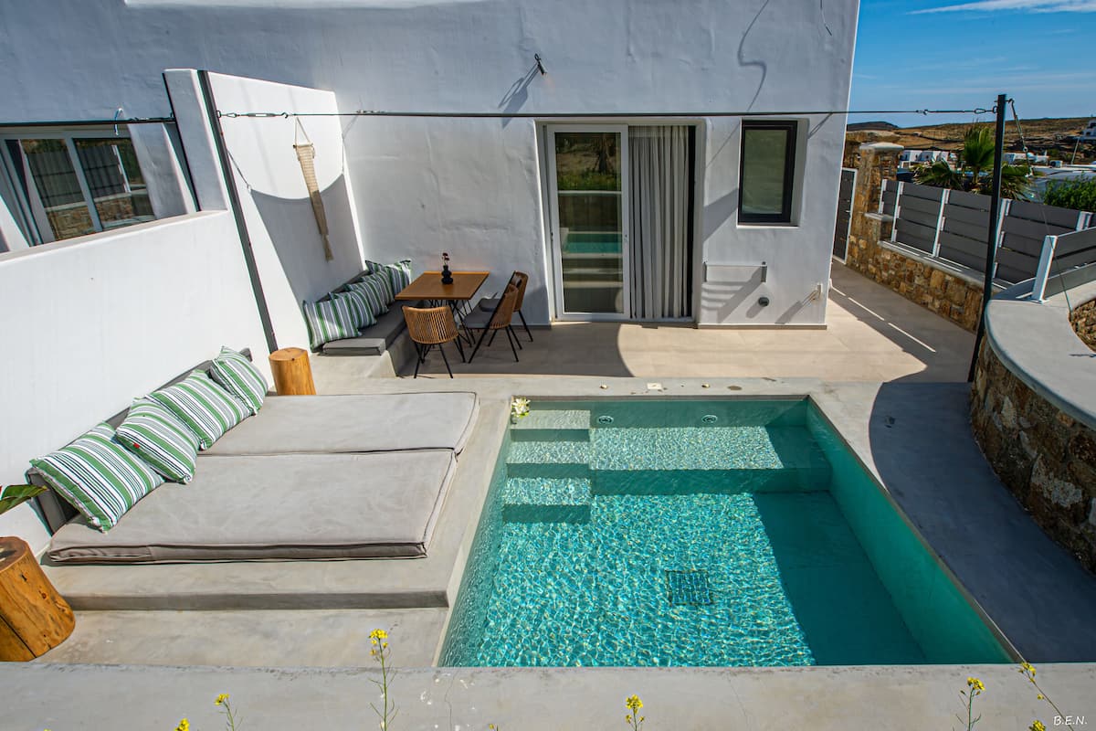 Uma área de piscina moderna ao ar livre, com espaço para sentar, uma mesa e uma porta de vidro deslizante que dá para um alpendre coberto.