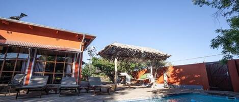 Piscina com espreguiçadeiras e uma estrutura de telhado de palha.