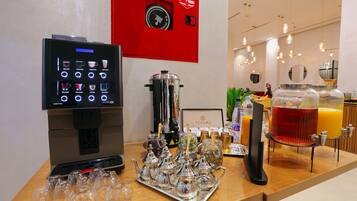 Uma máquina de café com diversas opções de bebidas, um tabuleiro com copos e um espaço para chá com bules.