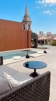 Terraço no telhado com piscina, área de estar e vista para uma torre de igreja.