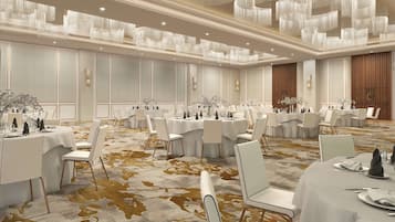 Uma ampla sala de banquetes com mesas redondas, cadeiras brancas e lustres.