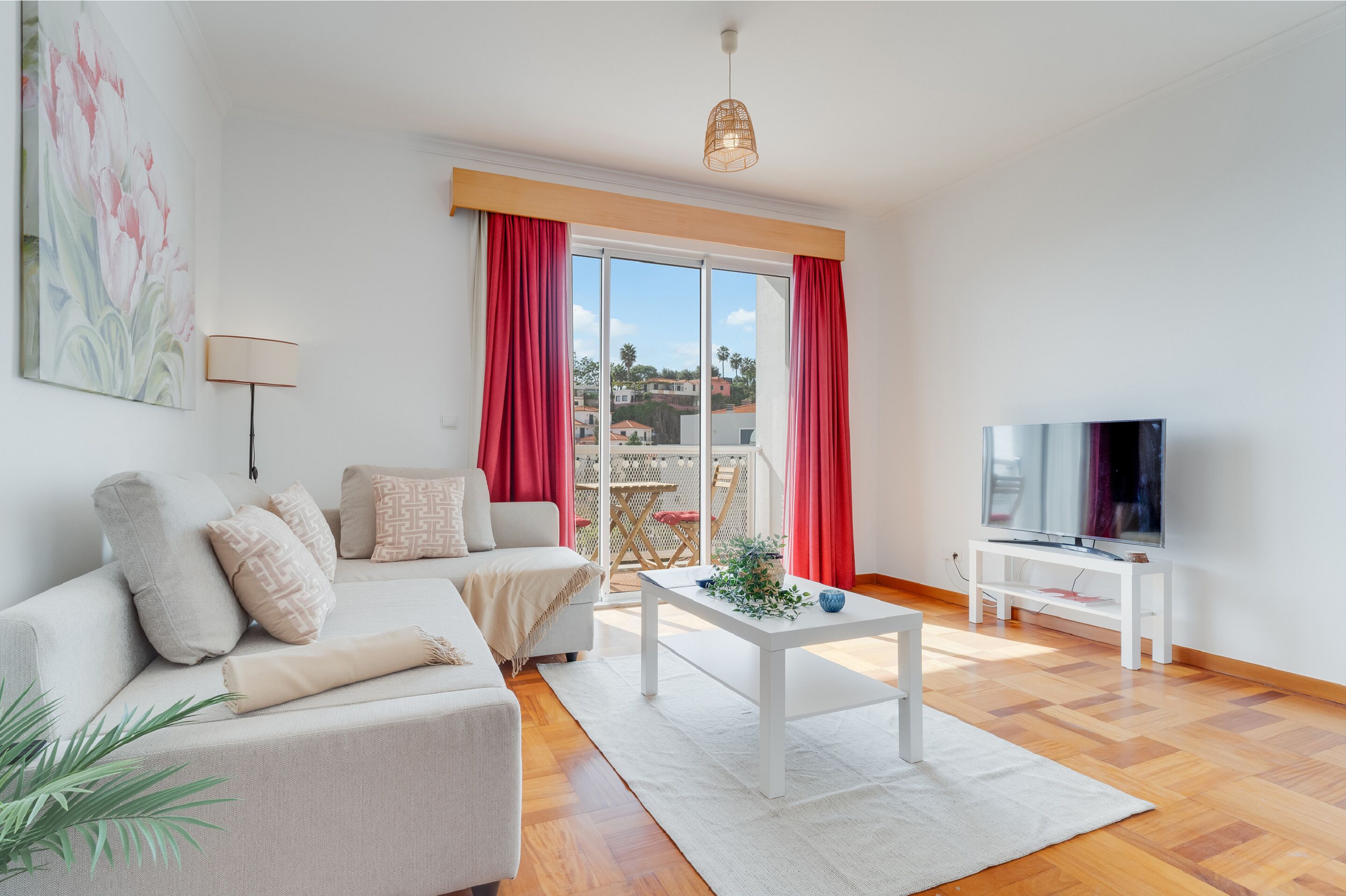 Uma sala de estar moderna com sofá, mesa de centro, televisão e porta de vidro deslizante com cortinas vermelhas.