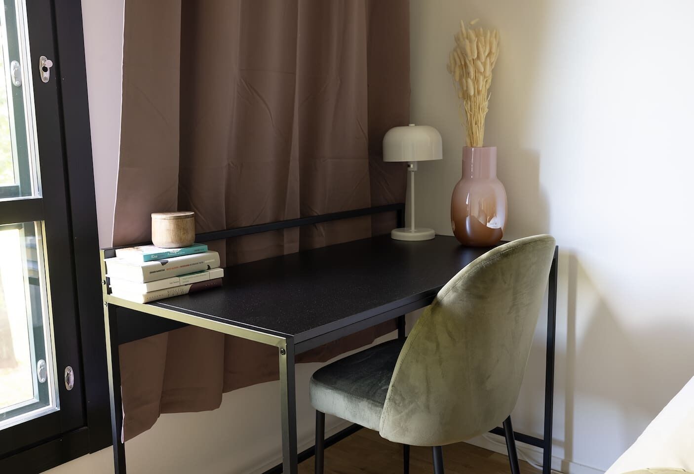 Quarto com escrivaninha, cadeira, livros, luminária e um vaso com plantas secas.