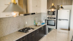 Uma cozinha moderna com armários escuros, bancada de granito, fogão a gás, forno, micro-ondas e geladeira.