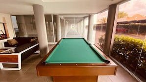 Uma mesa de bilhar em uma sala moderna, com um corredor longo e janelas amplas.