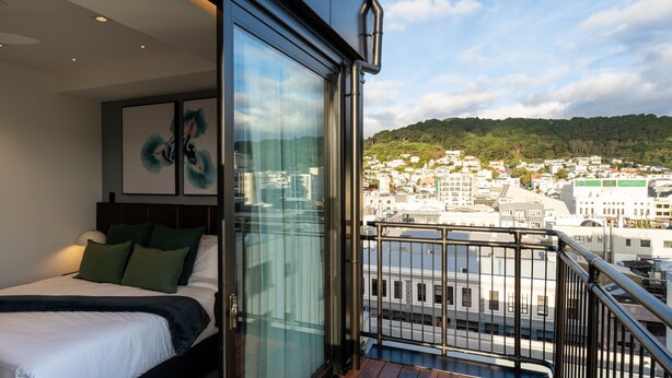 Quarto moderno com uma cama grande, porta de vidro que dá para uma varanda com vista da cidade.