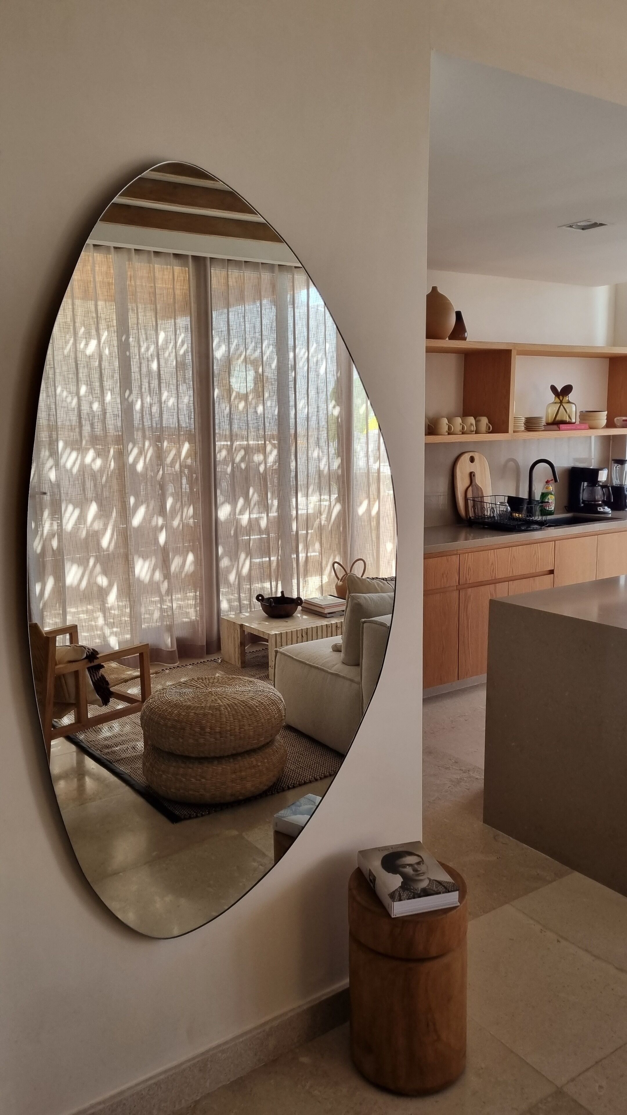 Uma sala de estar moderna com um espelho grande, um banquinho redondo de madeira, um sofá e uma mesa de jantar.