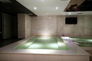 Uma área de spa com uma banheira de hidromassagem grande e retangular e outra menor, ambas com jatos de água.