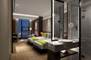 Quarto de hotel moderno com cama grande, área de estar separada, banheiro com espelho amplo e vista para a cidade.