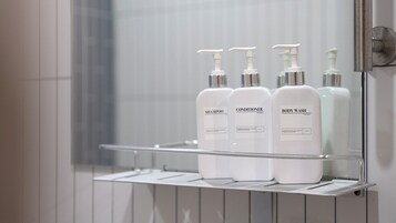 Uma prateleira no banheiro com três frascos de produtos de higiene pessoal: shampoo, condicionador e sabonete líquido.