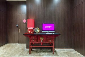 Um lobby de hotel moderno com uma parede de madeira, uma mesa vermelha com um computador e uma placa rosa que indica uma academia.