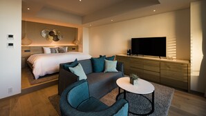 Quarto de hotel moderno com cama, sofá, televisão e uma pequena mesa.