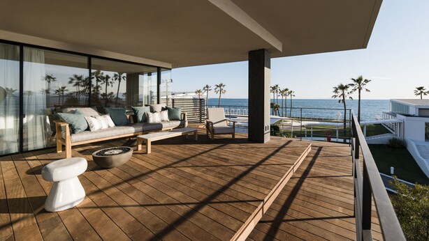 Uma área externa moderna com deck de madeira, um sofá, uma poltrona e uma mesa de centro.