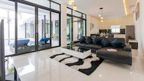 Uma sala de estar moderna com divisória de vidro, um tapete preto e branco, sofá preto e uma mesa de centro de vidro.
