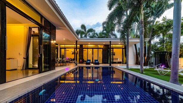 Uma área de piscina moderna com chão em mosaico, portas de vidro e mobiliário para área externa.
