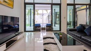 Uma sala de estar moderna com uma TV de tela plana, uma mesa de centro de vidro, um sofá de couro preto e uma grande porta de vidro deslizante que dá para um espaço ao ar livre.