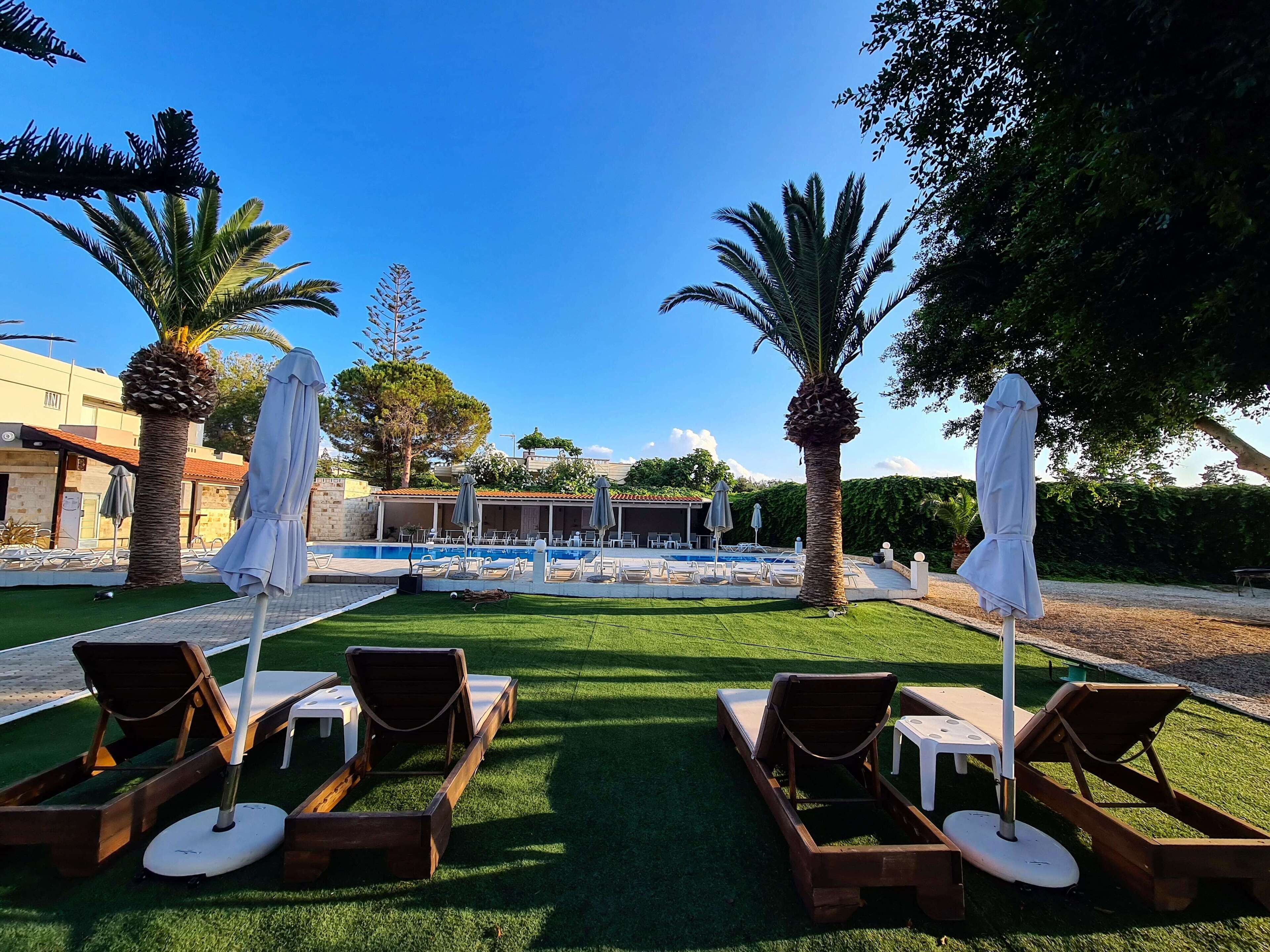 Área da piscina com espreguiçadeiras e guarda-sóis, uma piscina e um edifício ao fundo.
