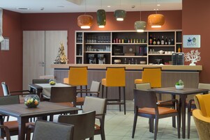 Um restaurante com várias mesas e cadeiras, um espaço de bar e prateleiras repletas de garrafas e copos.