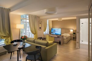 Quarto de hotel moderno com sofá, mesa de jantar, televisão e cama.
