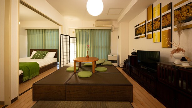 Quarto com cama, sofá, televisão e mesa com almofadas.