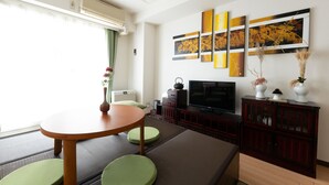 Uma sala de estar moderna com um sofá, uma mesa de jantar e uma televisão. Há peças decorativas nas paredes e um armário.
