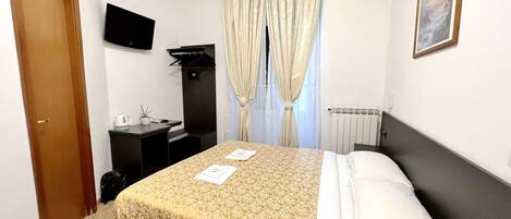 Um quarto com cama, escrivaninha, cadeira, televisão e radiador.