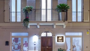 Entrada de um hotel com porta de madeira, varanda com plantas e um cartaz grande na parede.