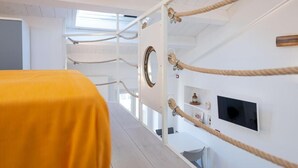 Quarto com cama, televisão e janela com detalhes em corda.