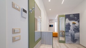 Quarto de hotel moderno com piso de madeira, uma escrivaninha com cadeira, uma cama com colcha laranja e um espelho grande.