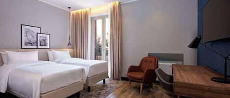 Quarto de hotel com duas camas, uma escrivaninha, uma cadeira e uma televisão.