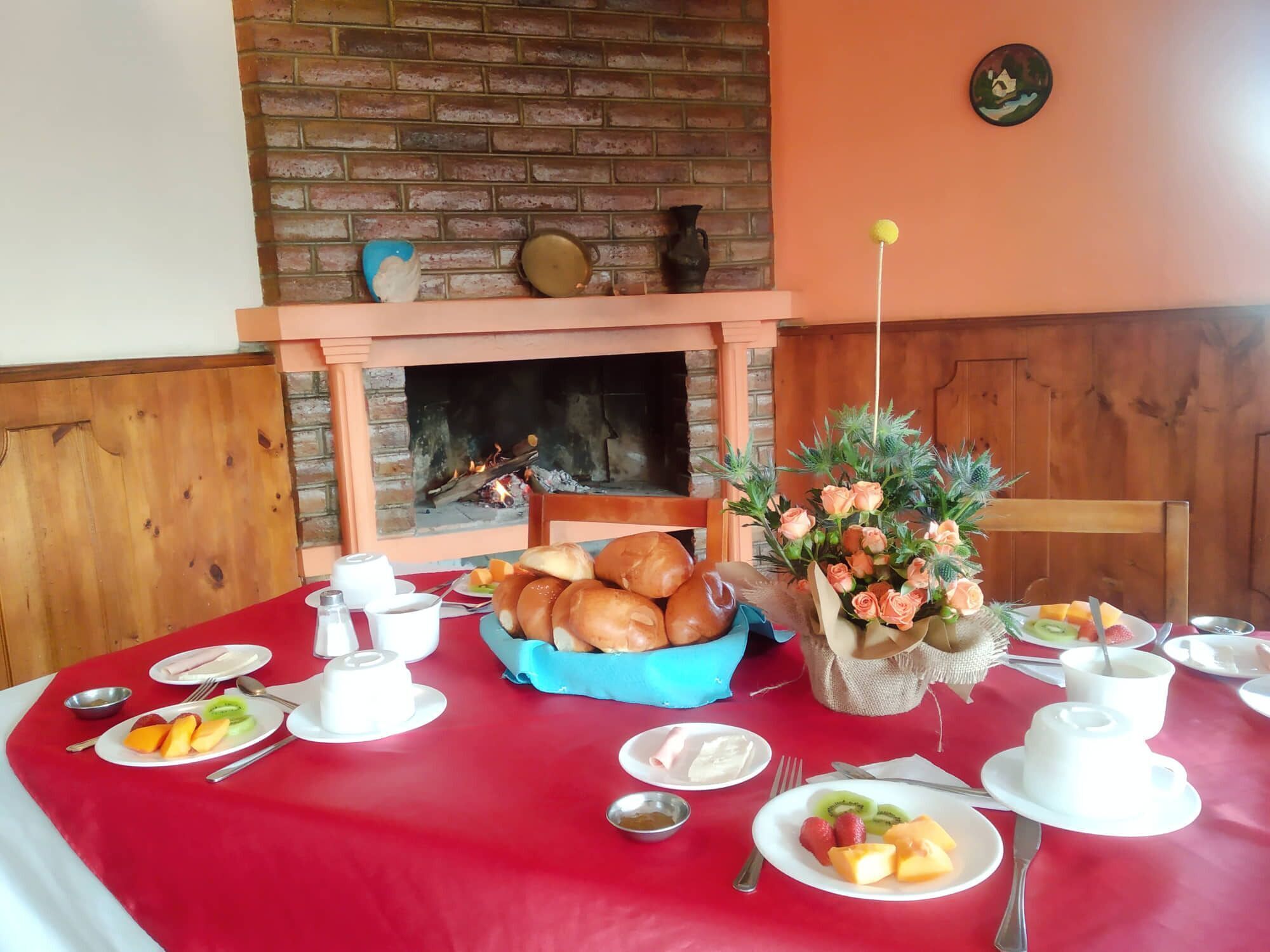 Uma mesa de jantar posta com pratos de fruta, pão e um vaso de flores.