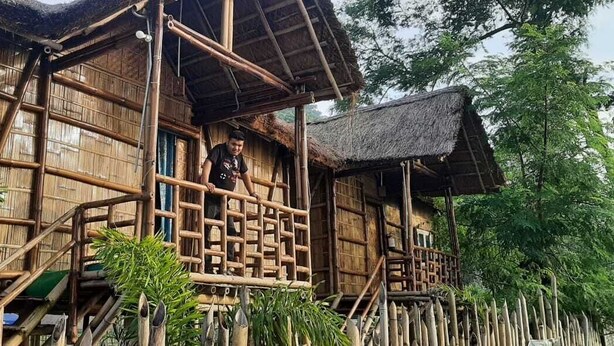 Uma casa tradicional de bambu com telhado de palha, varanda de madeira e uma janela.