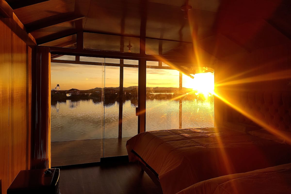 Quarto com uma grande janela com vista para a água e um pôr do sol.