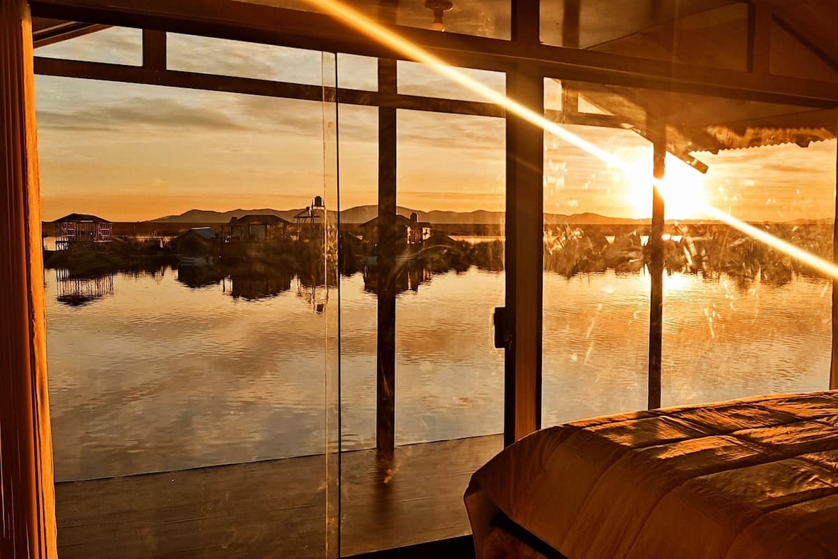 Quarto com uma janela grande, uma cama e vista para a água e edifícios.