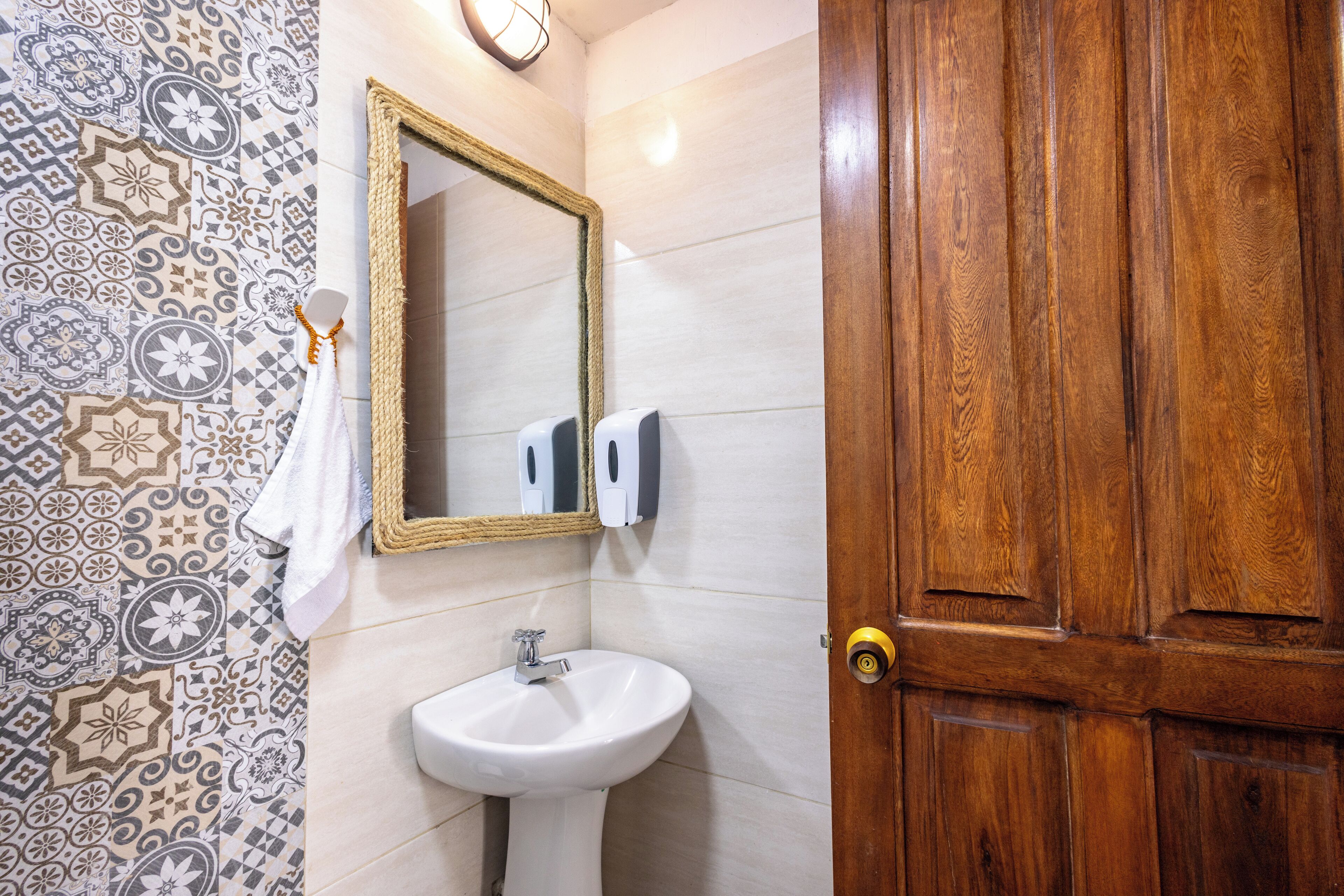 Um banheiro com parede de azulejos estampados, pia branca, espelho com moldura de madeira, toalha pendurada em um suporte e porta de madeira.