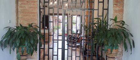 Paredes de tijolo com um portão de metal, plantas em vasos e um chão de azulejos.