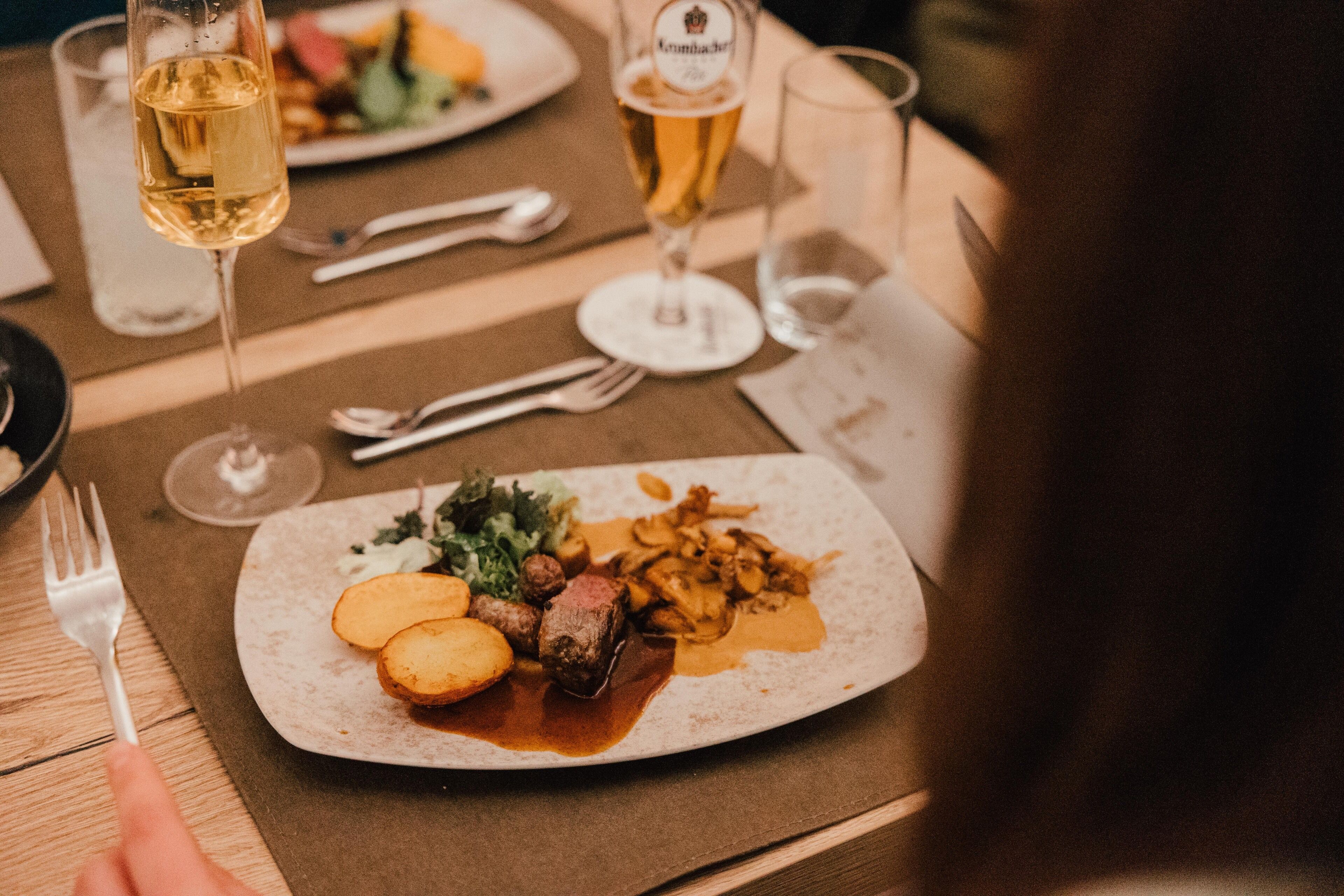 Uma mesa de jantar com pratos de comida, copos de vinho e talheres.