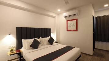 Quarto de hotel com cama, mesa de cabeceira, luminária, ar-condicionado e um quadro na parede.