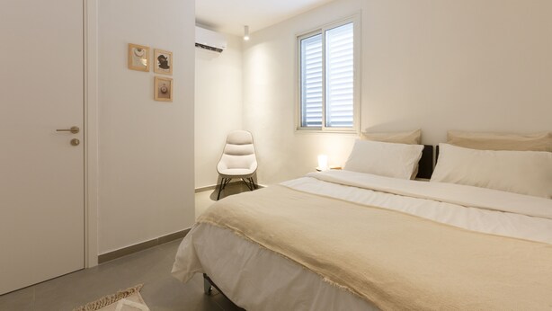 Um quarto com uma cama, uma cadeira, uma janela com persianas e uma porta.