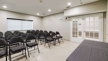 Uma sala de conferência com fileiras de cadeiras, uma tela de projeção e uma mesa grande.