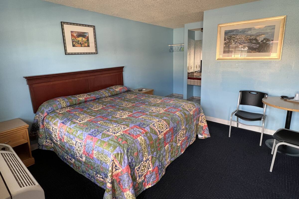 Quarto de hotel com cama, secretária, cadeira e espelho de casa de banho.