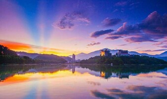 Vista serena de um lago, com um edifício semelhante a um castelo no topo de uma colina, refletindo em águas calmas.