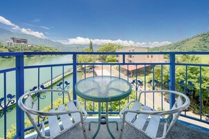 Varanda com mesa de vidro e duas cadeiras, com vista para um rio e uma paisagem montanhosa.