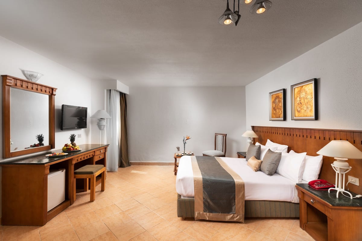 Quarto de hotel com cama, escrivaninha, cadeira e televisão na parede.